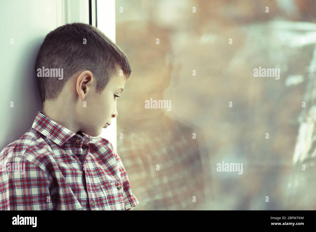 Sad boy sitting near window Stock Photo - Alamy