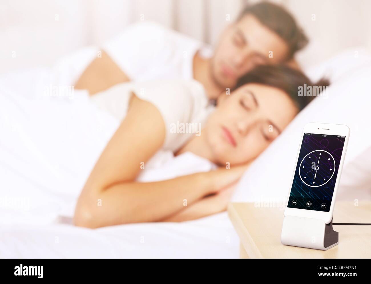 Happy couple waking up with mobile alarm clock Stock Photo - Alamy
