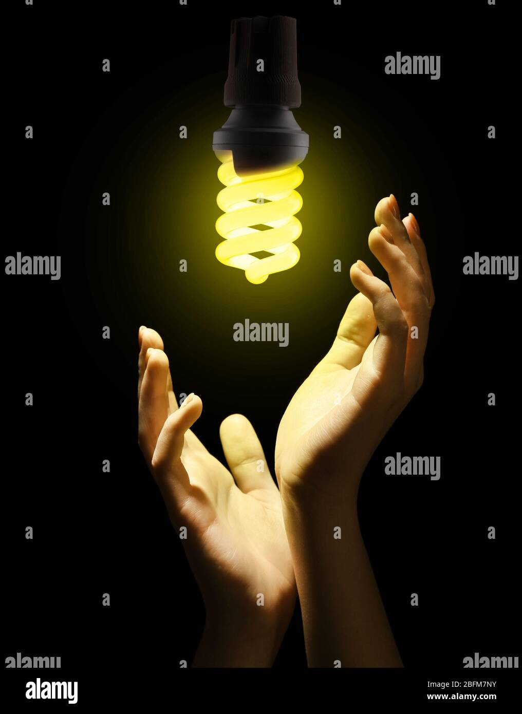 Hands with energy saving light bulb on black background Stock Photo - Alamy