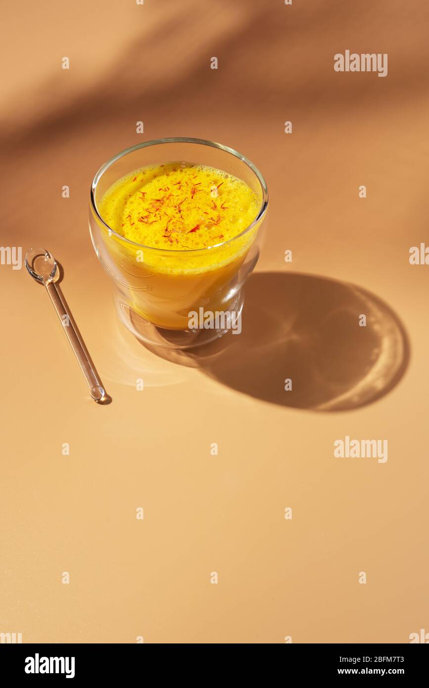 Saffron latte in a glass cup on a beige background, golden milk, hard ...