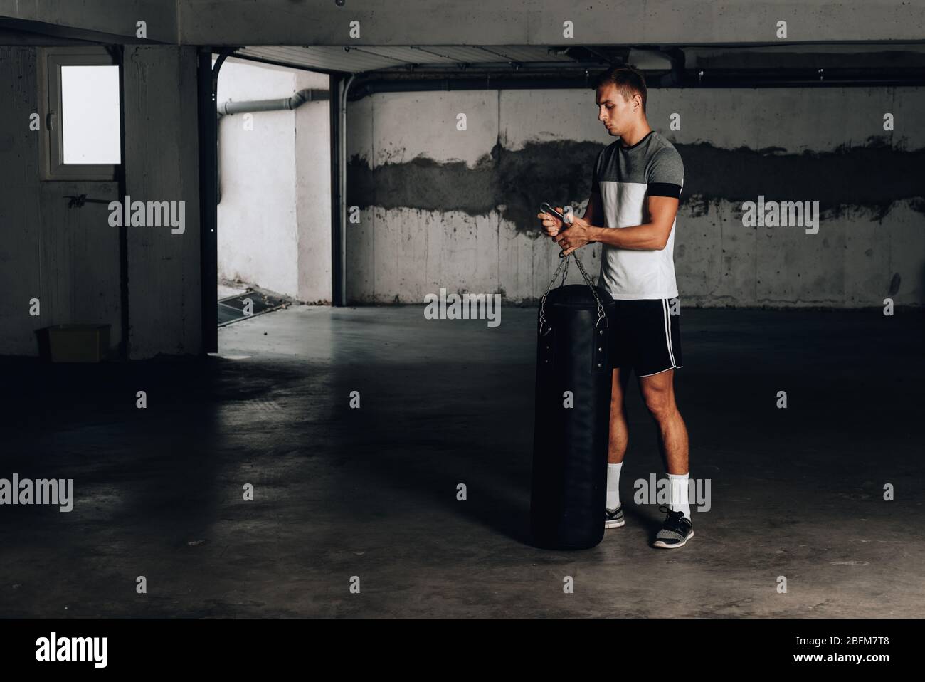 Sporty man set up boxing bag on the wall in underground garage Stock ...