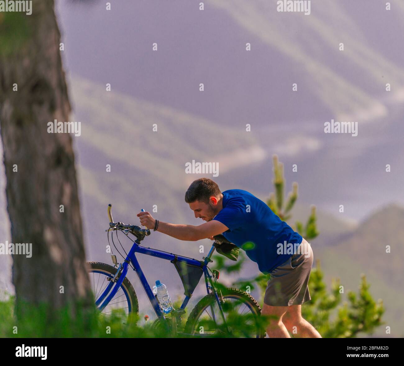 Tired cyclist is wiping his sweat off his face while pushing his ...