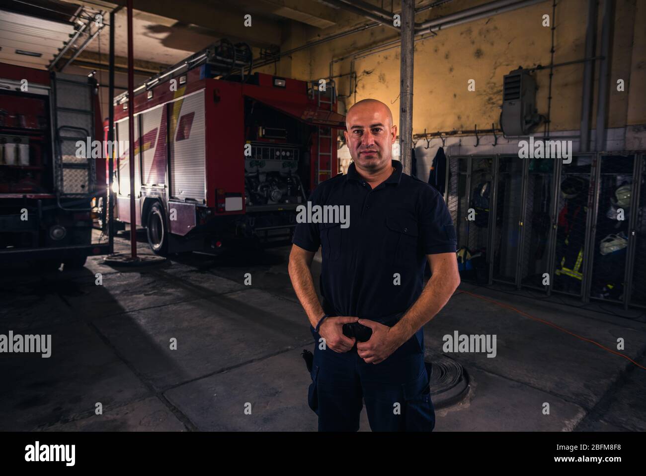 Portrait of handsome firefighter standing against trucks at fire ...