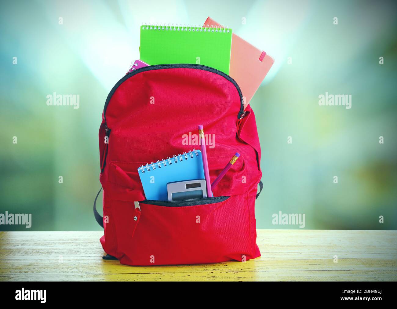 Red bag with school equipment on wooden table in classroom Stock Photo ...