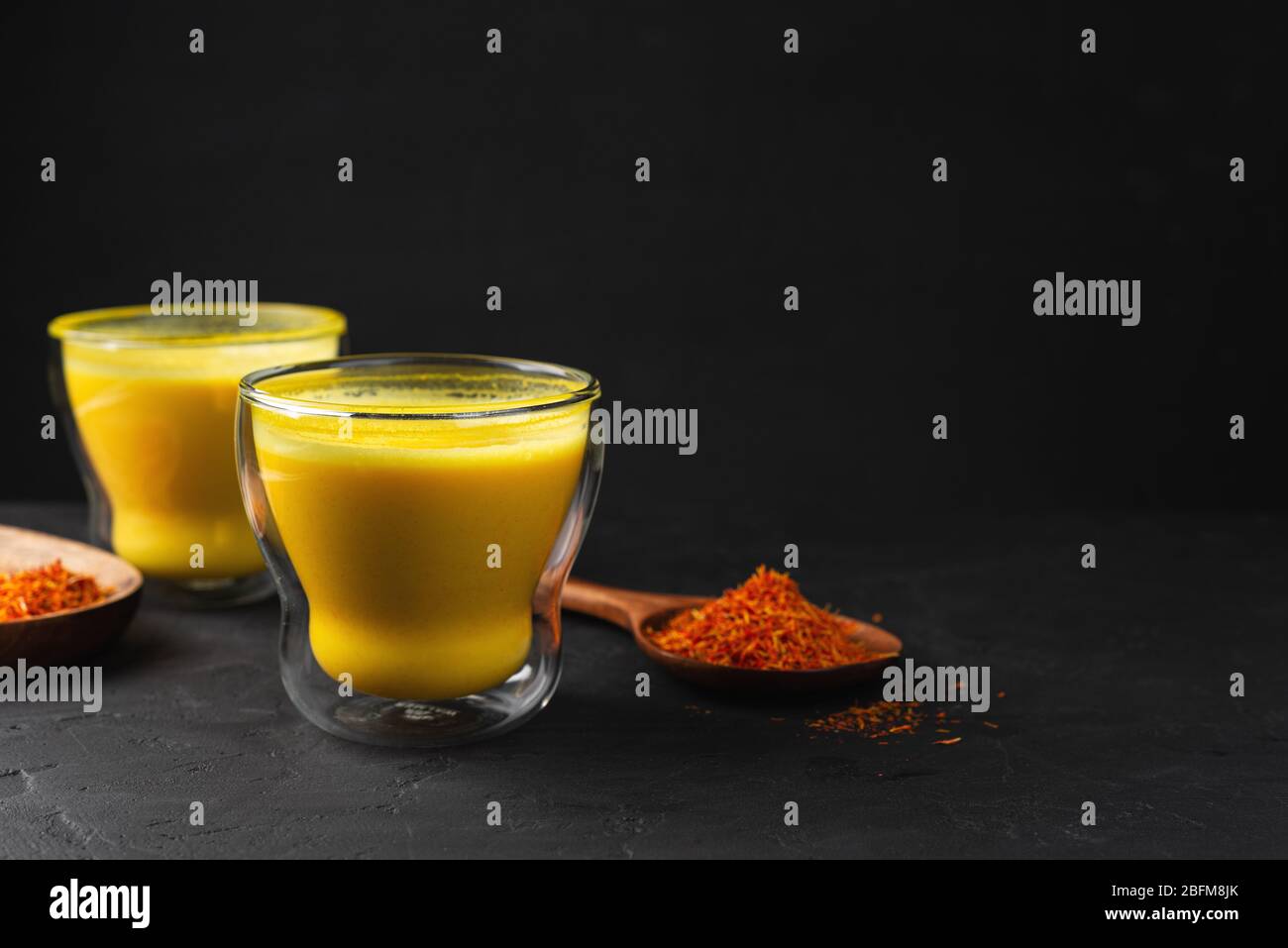 Saffron latte in a glass cup on a black concrete background, dry spice ...