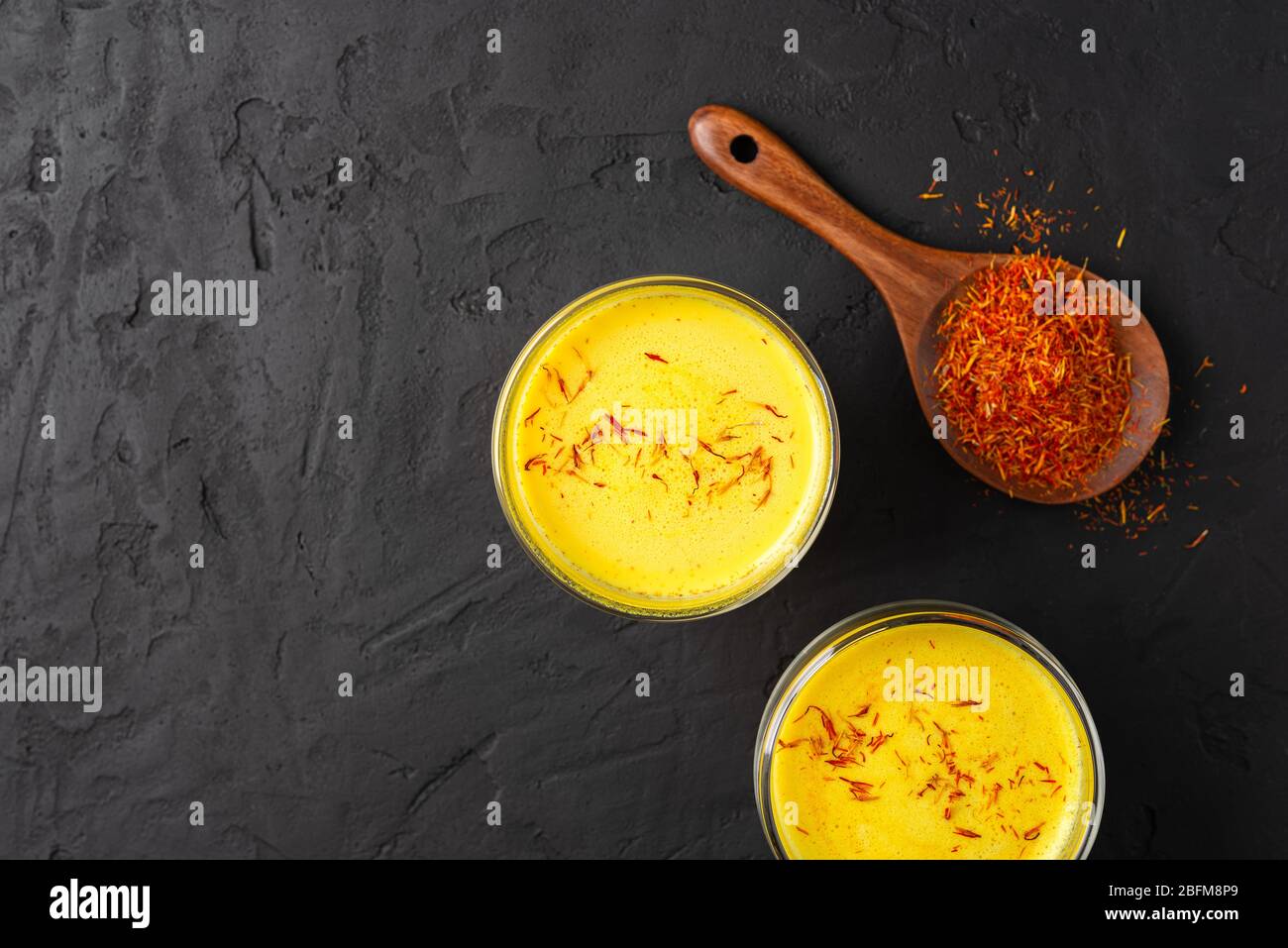 Saffron latte in a glass cup on a black concrete background, wooden ...