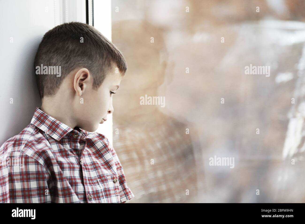 Sad boy sitting near window Stock Photo - Alamy