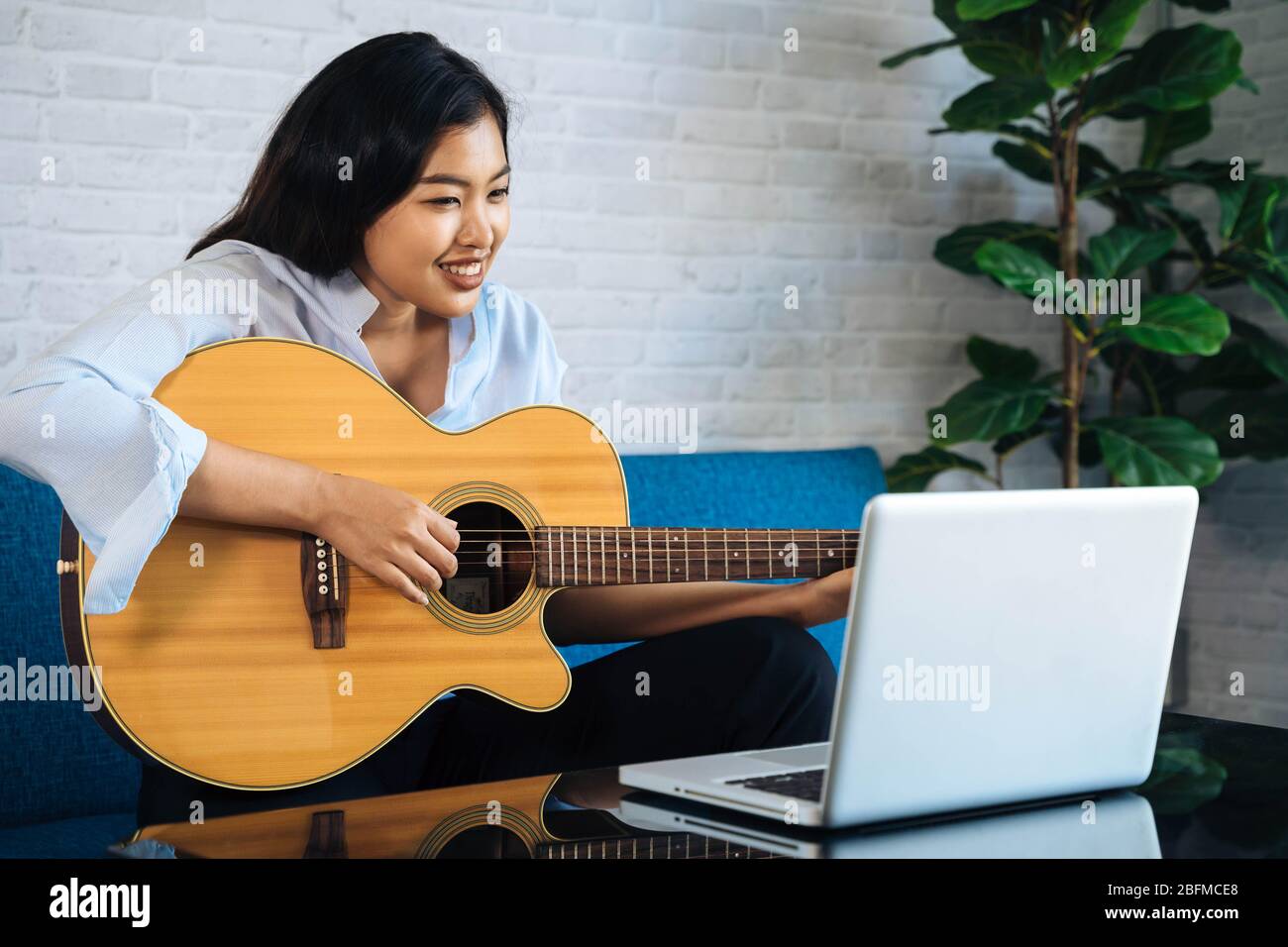 Young Asian woman practicing and learning how to play guitar on laptop ...