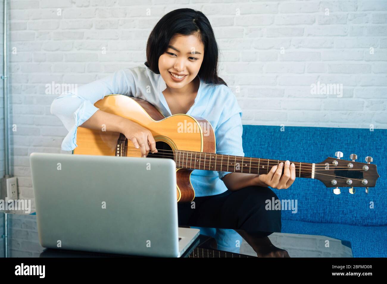 Young Asian woman practicing and learning how to play guitar on laptop ...