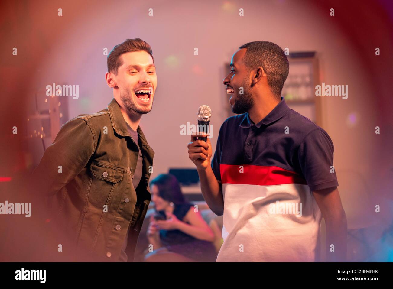 Two cheerful intercultural guys singing together in microphone while ...