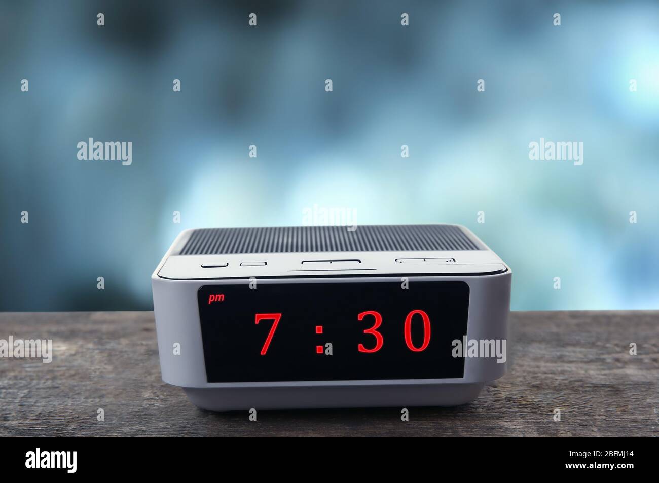 Digital clock showing 7:30 o'clock on wooden table, night background ...