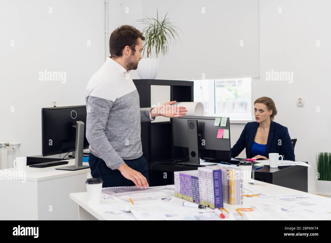 Male office worker approaching his female colleague to ask something ...