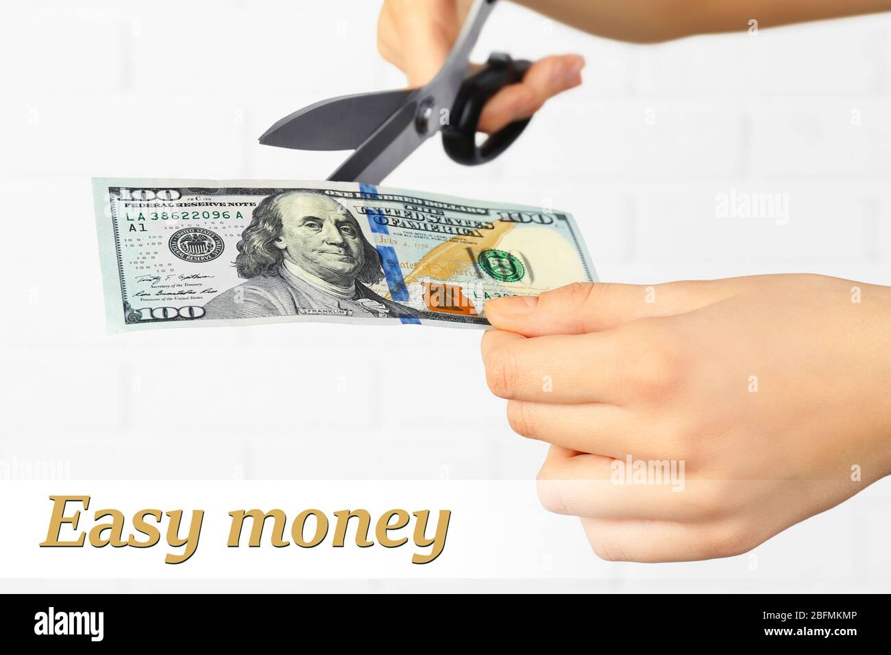 Hands with scissors cutting money on white brick wall background Stock ...