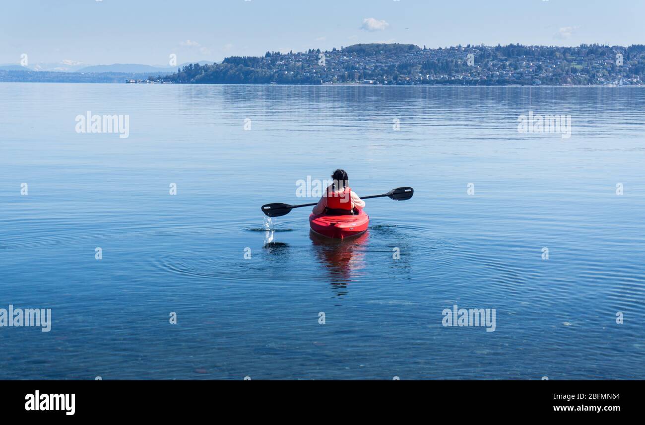 A lone kayaker in a bright red kayak explores the Puget Sound on a calm ...