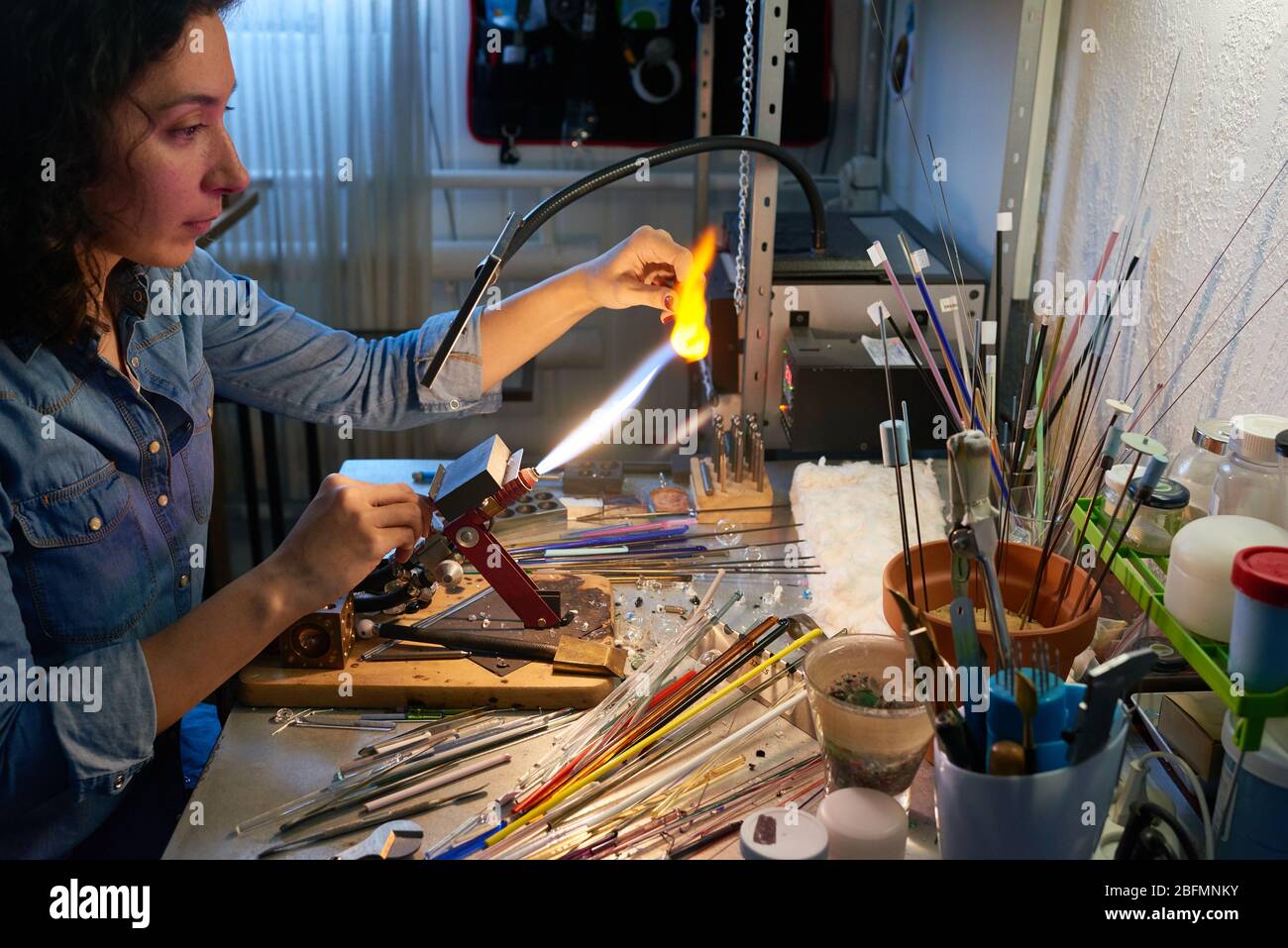 Young creative female lampworking master burning glass workpiece in ...