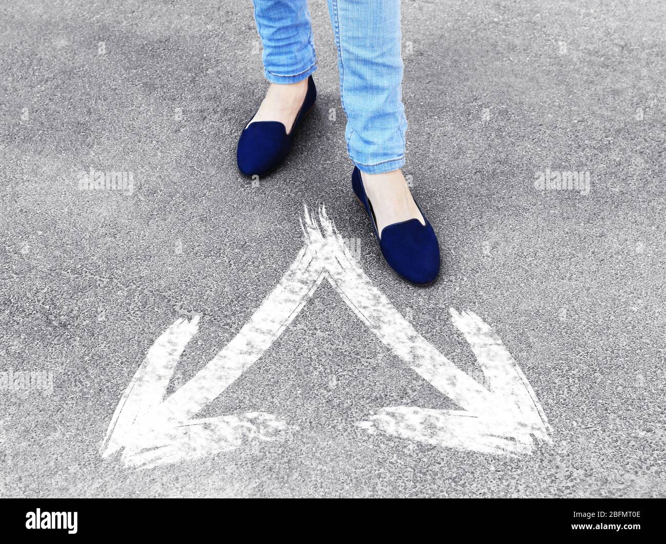 Female feet standing on road with white arrows Stock Photo - Alamy