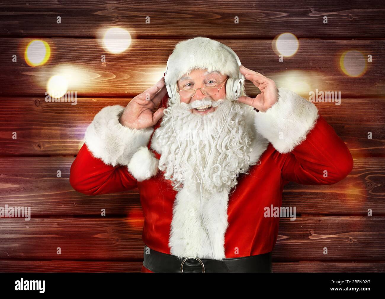 Santa Claus listening to music against wooden background with lights on ...