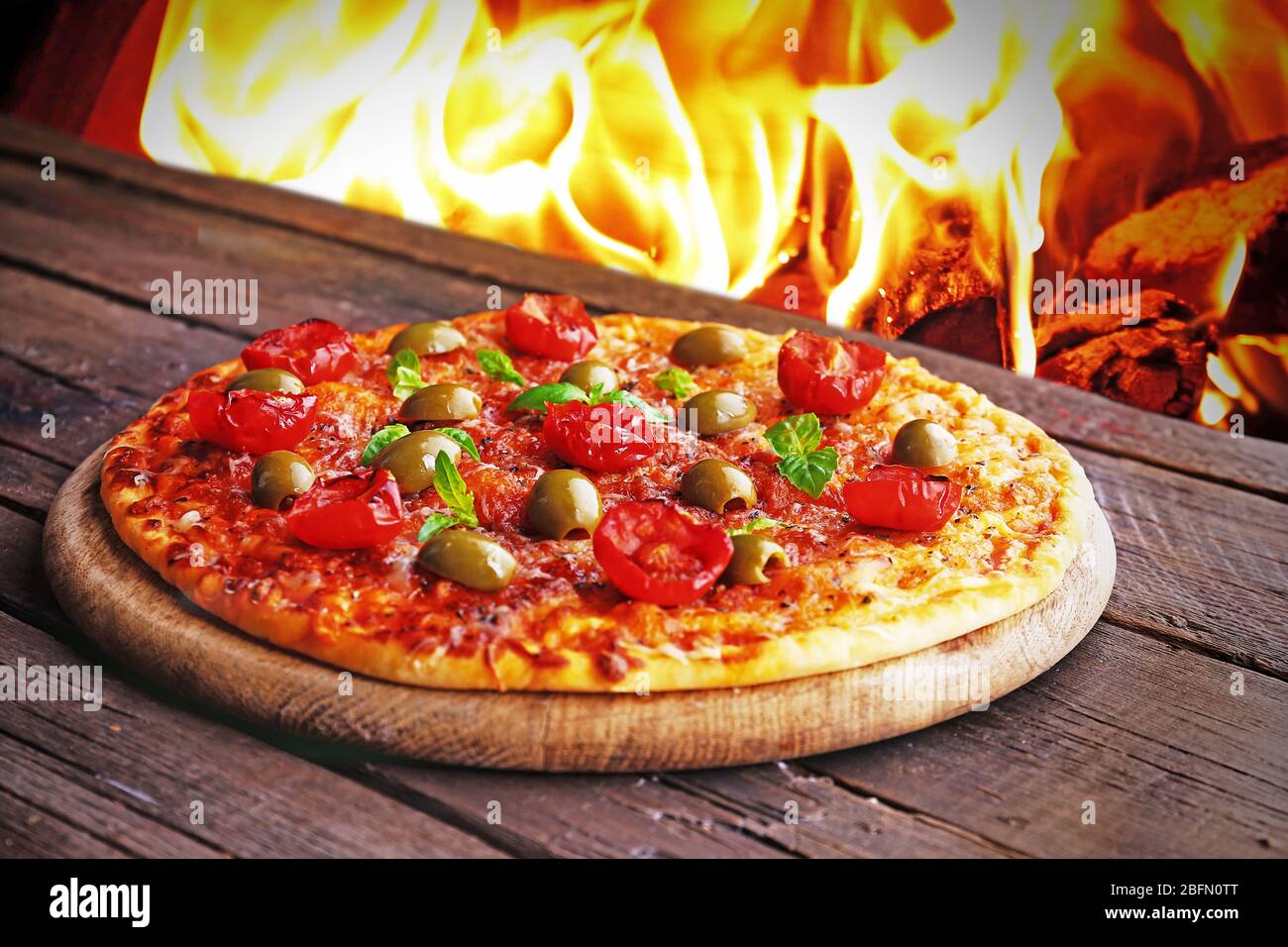 Tasty hot pizza with cherry tomatoes on wooden table on fire flame ...