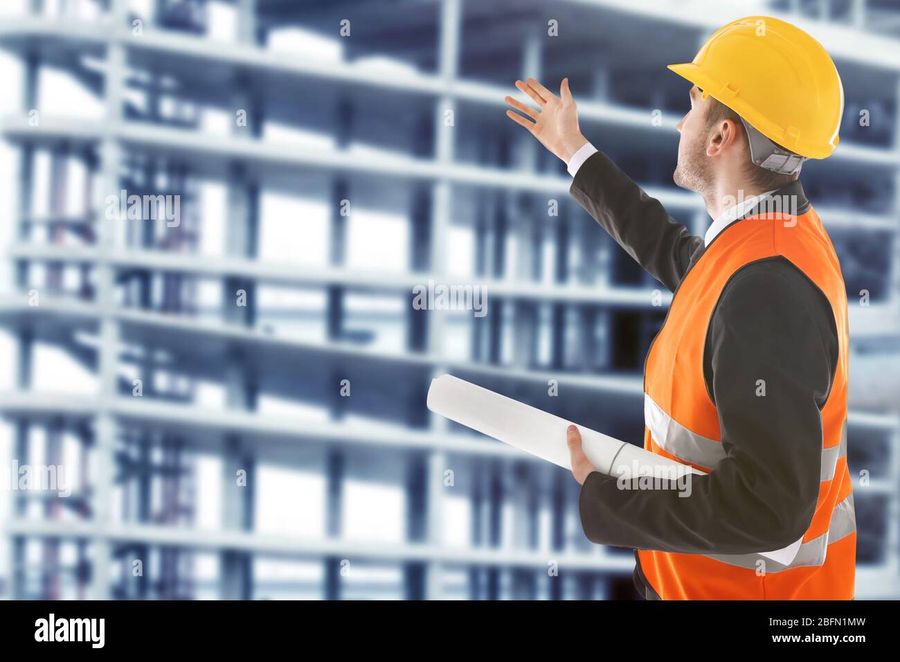 Professional engineer with blueprint on blurred construction site ...