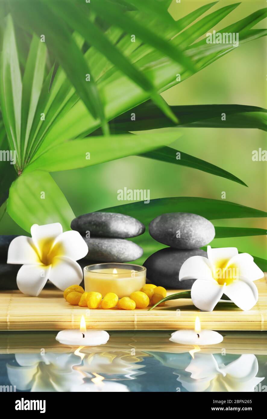 Composition with spa stones and flowers on green palm leaves background ...