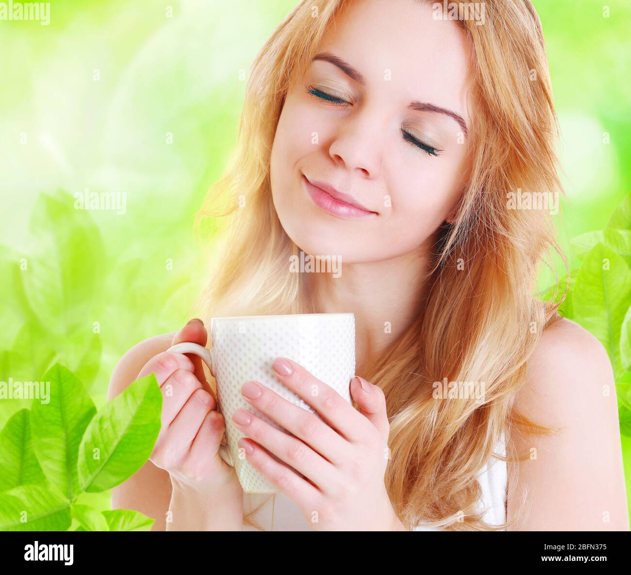 Beautiful girl enjoying a cup of tea on blurred green nature background ...