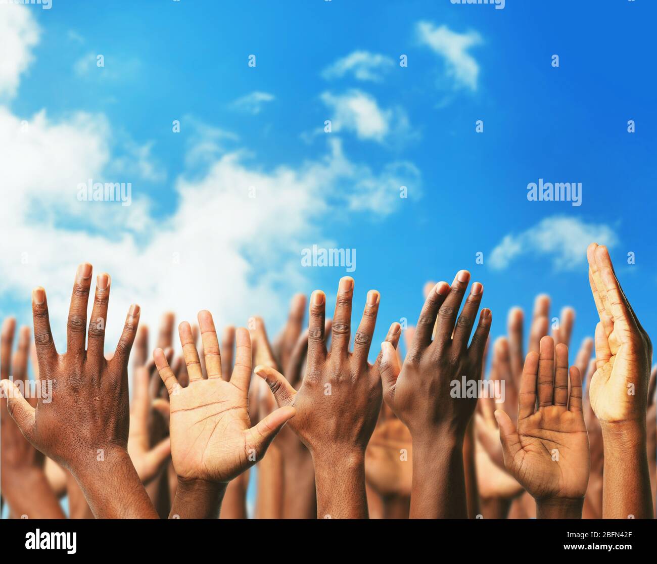 Crowd raising hands on blue sky background Stock Photo - Alamy