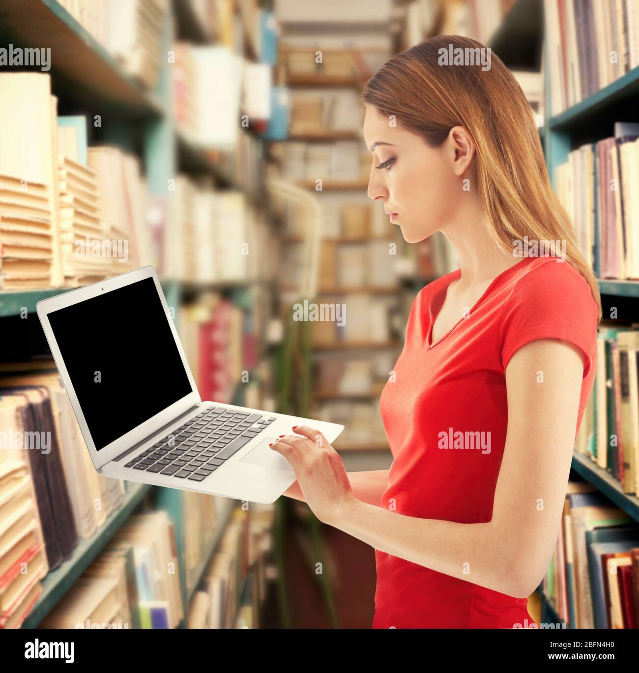 Young woman holding laptop in library Stock Photo - Alamy