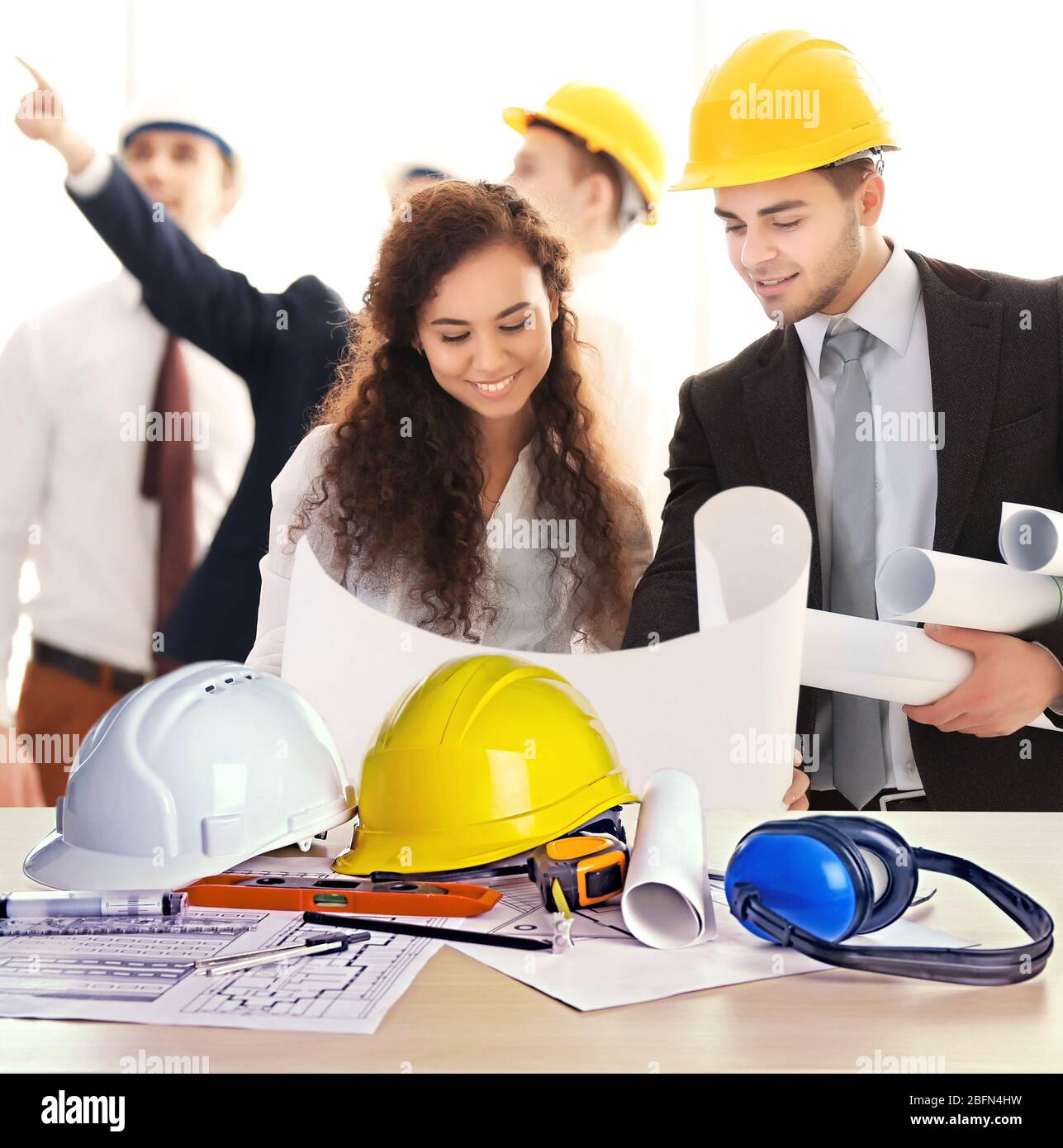 Table with construction drawings and few engineers with blueprint in ...