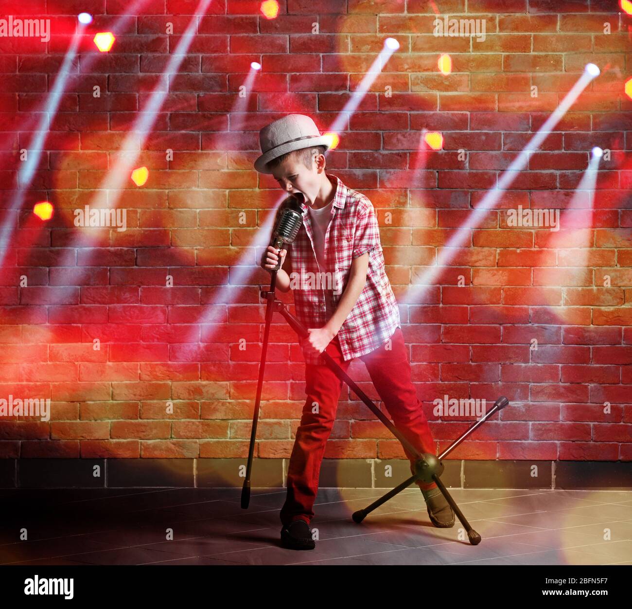Little boy singing with microphone and laser rays on brick wall ...