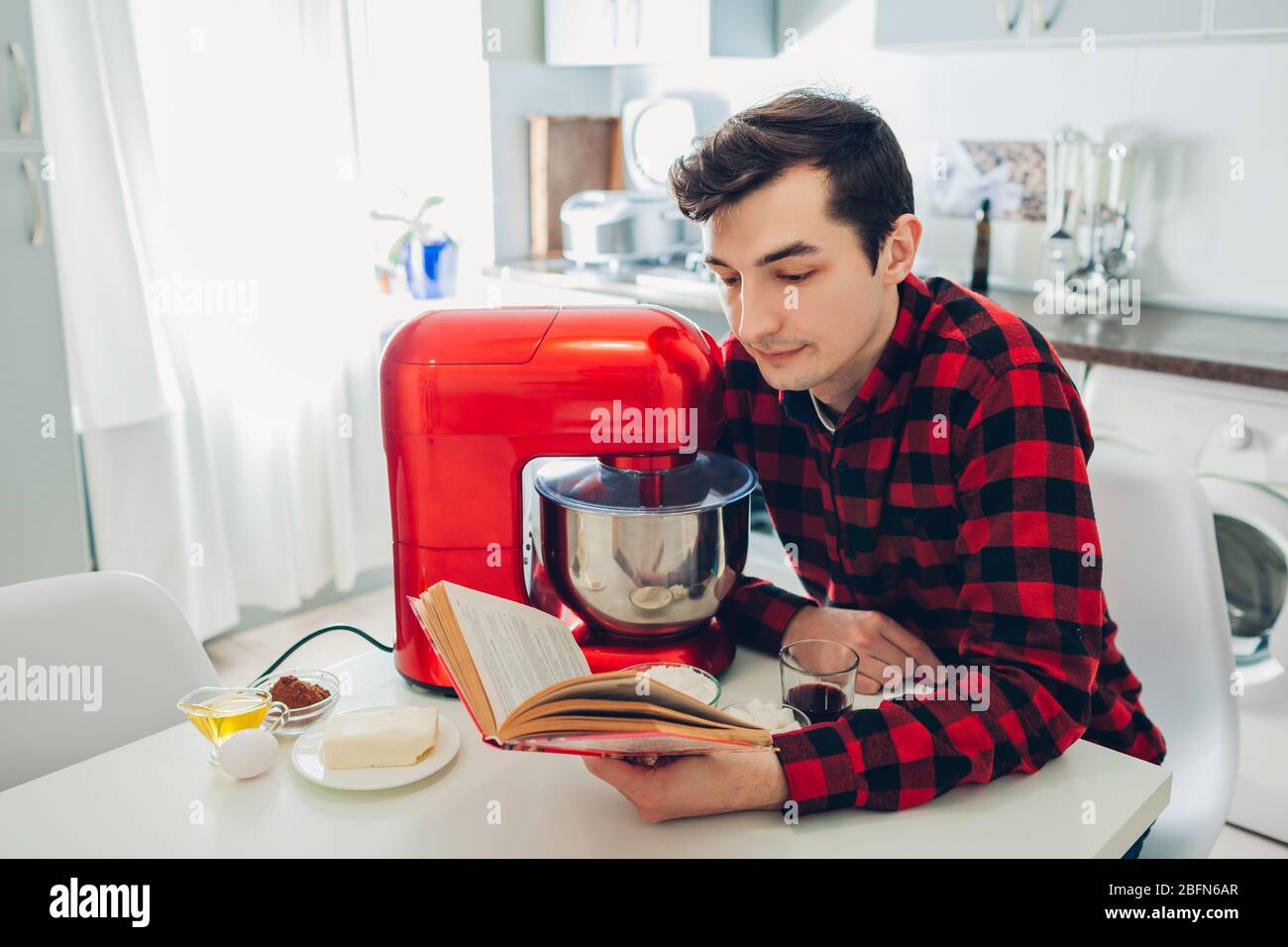 Young man reading recipe in culinary book. Guy learns to cooks pie with ...