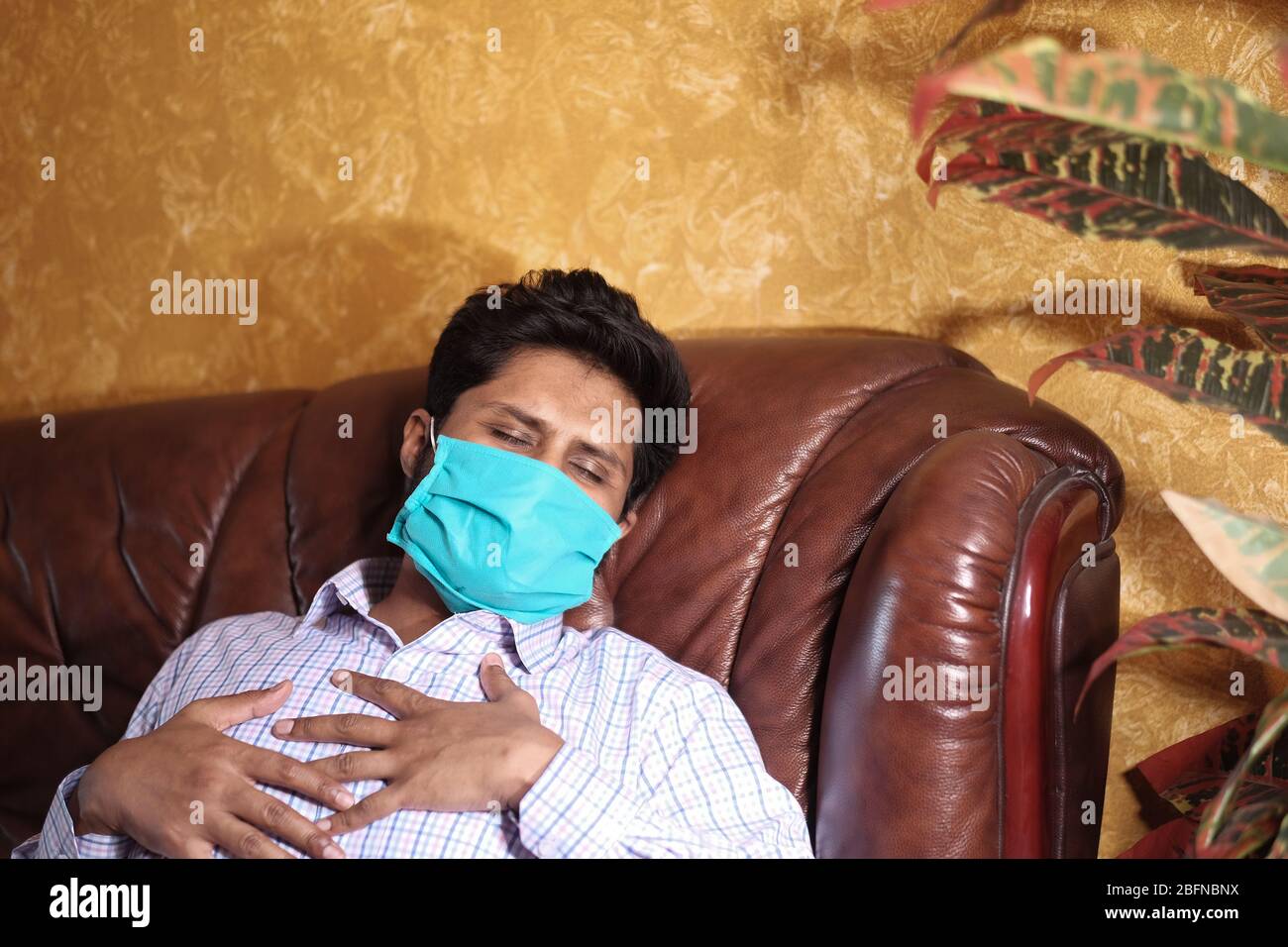 a sick man with a mask on his face sitting on sofa Stock Photo - Alamy