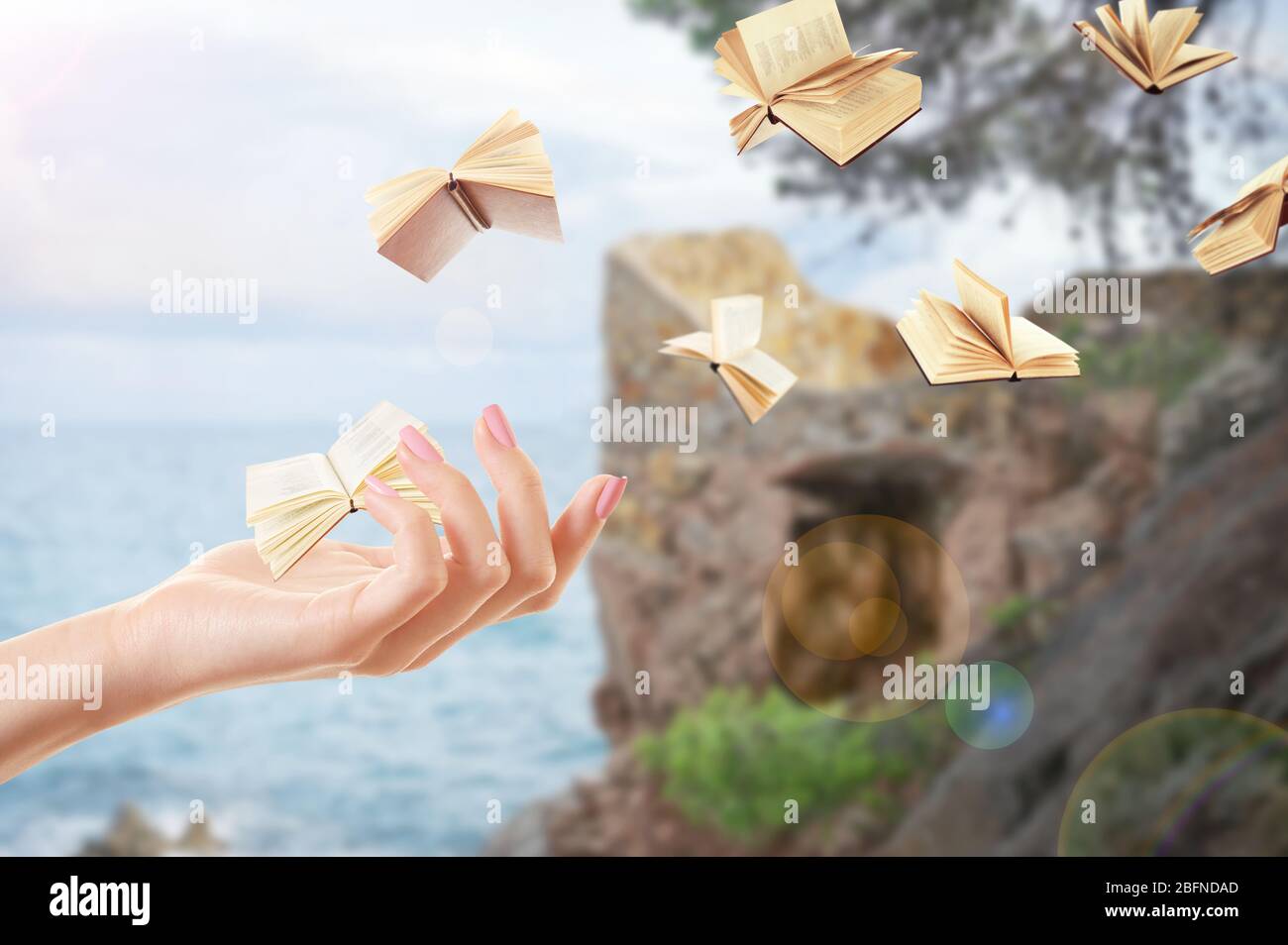 Female hand and flying books on landscape background Stock Photo - Alamy