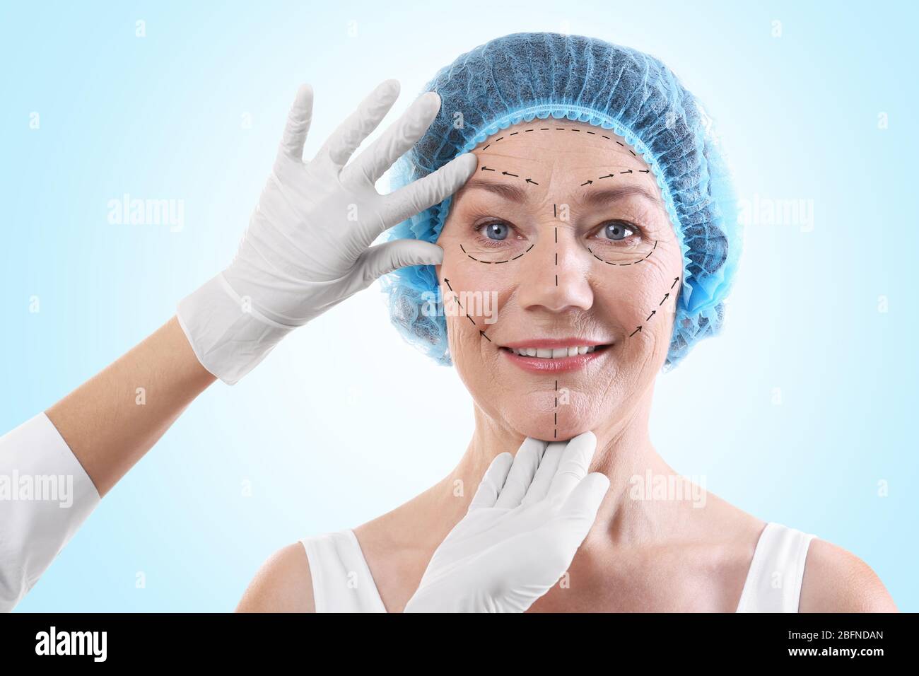 Surgeon examining female face against blue background. Plastic surgery ...