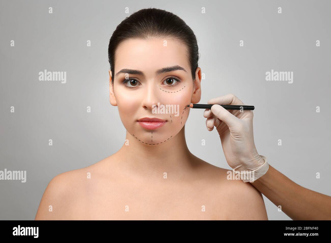 Surgeon drawing marks on female face against gray background. Plastic ...
