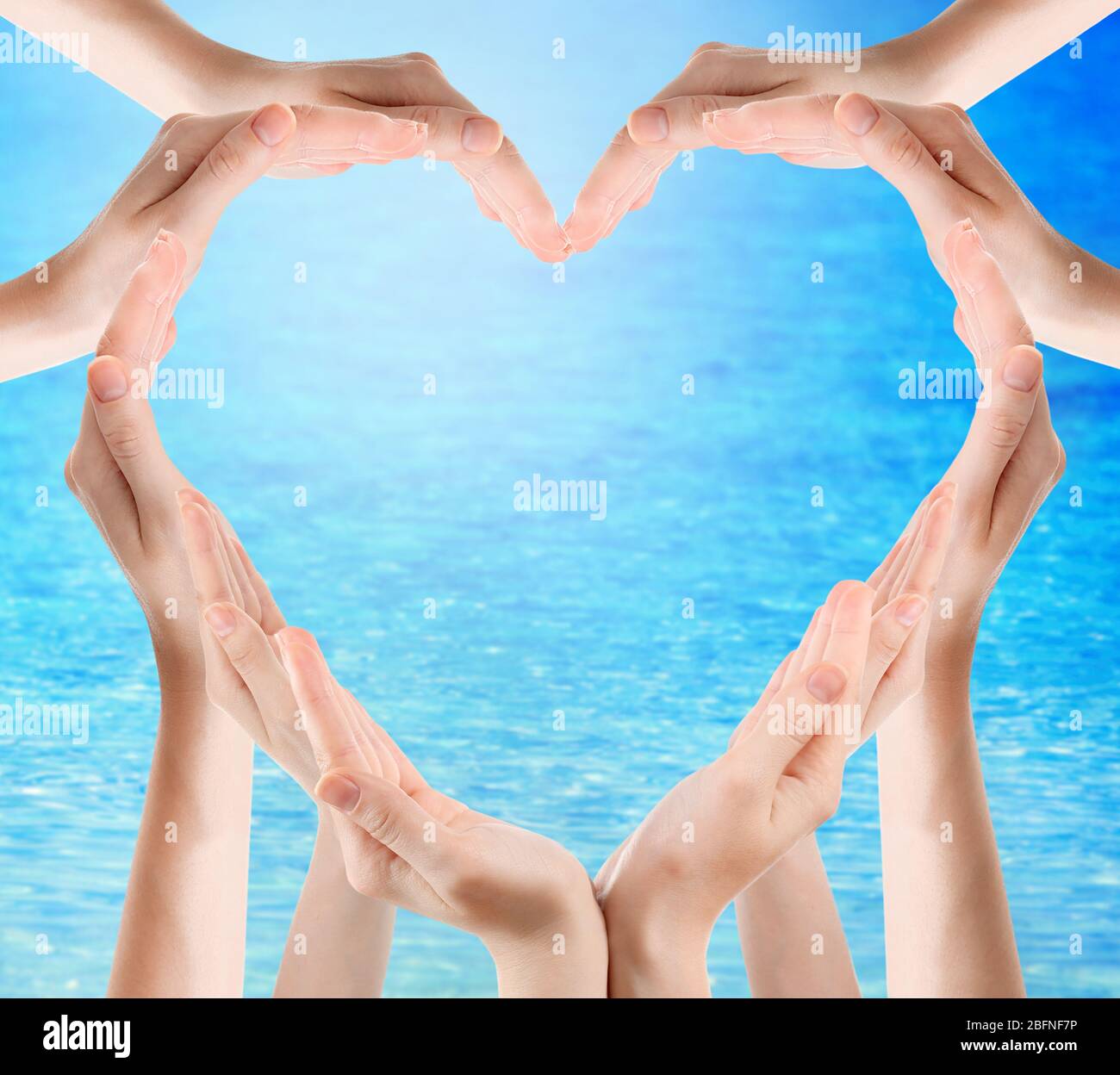 Collaborative human hands grouped in heart shape on water background ...