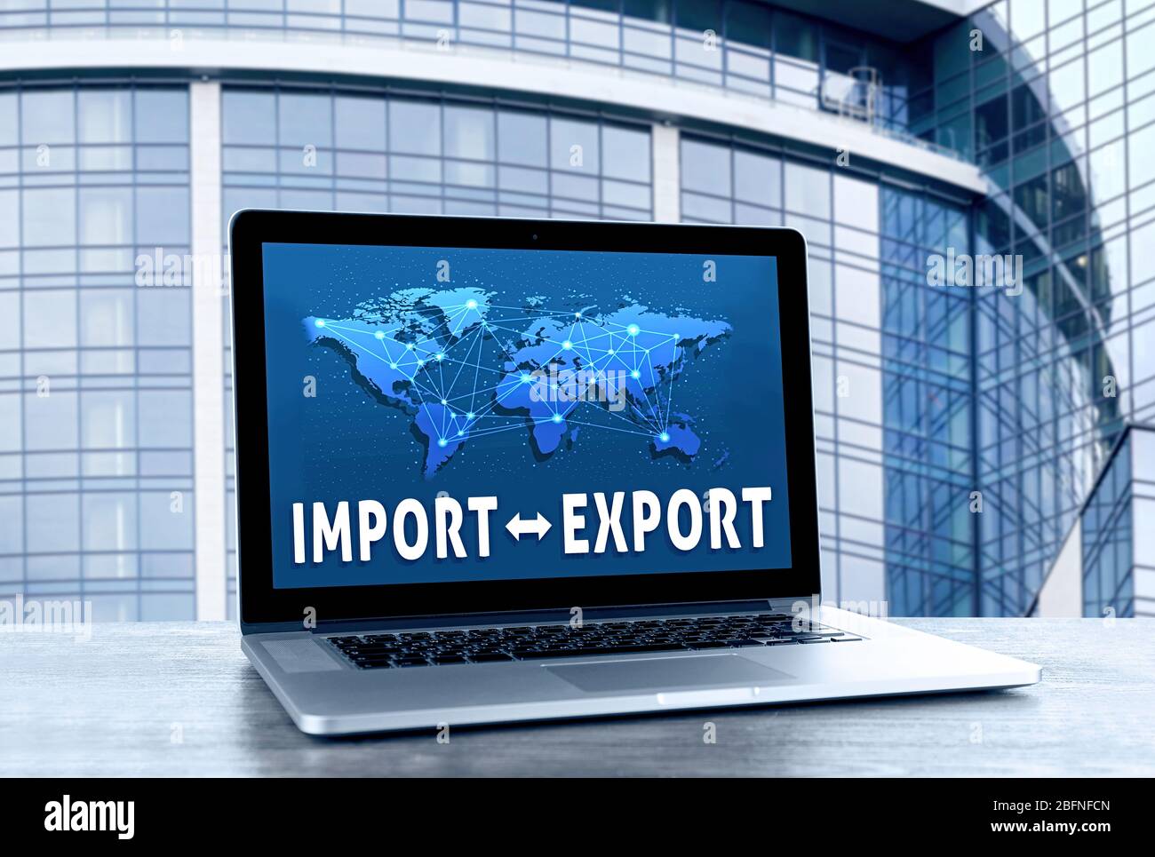 Laptop on table against building background. World map and text IMPORT ...