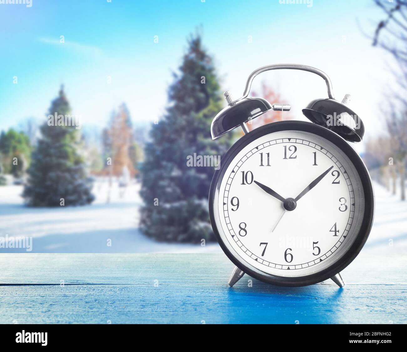 Alarm clock on wooden table against landscape background. Time change ...