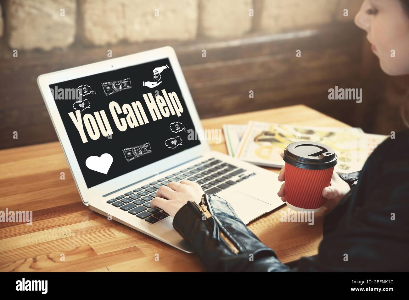 Young woman using laptop with text YOU CAN HELP on screen at table ...