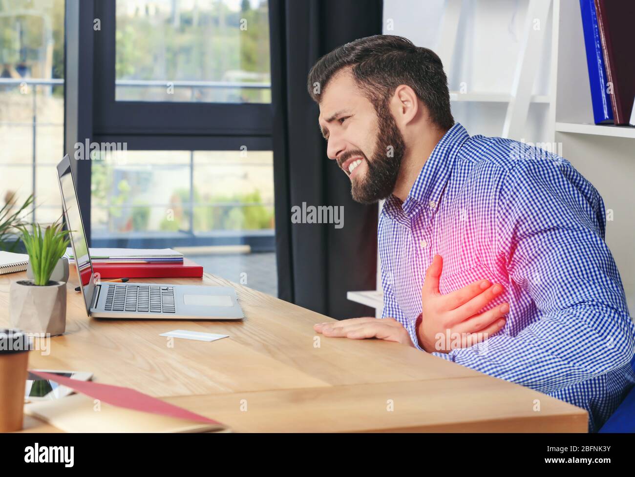 Young man suffering from chest pain in office Stock Photo - Alamy