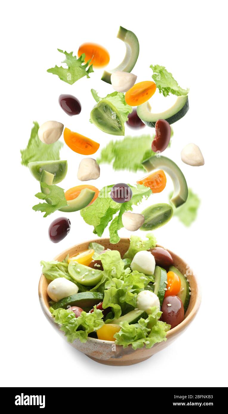 Sliced vegetables falling into bowl with salad on white background ...