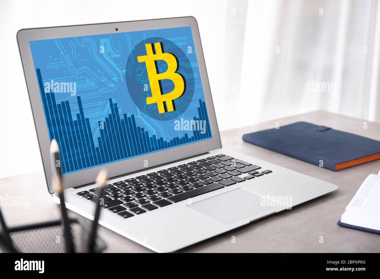 Modern workplace with laptop and bitcoin symbol on screen in office ...