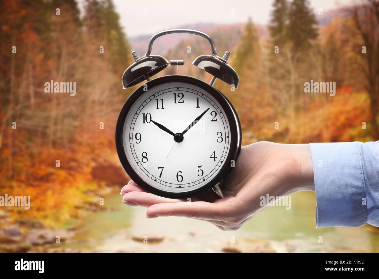 Female hand holding alarm clock on landscape background. Time change ...