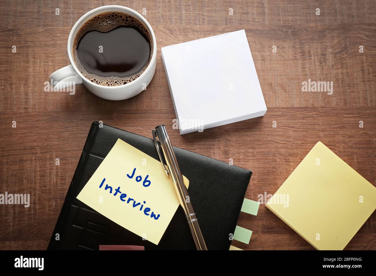 Note with text JOB INTERVIEW, cup of coffee and stationery on table ...