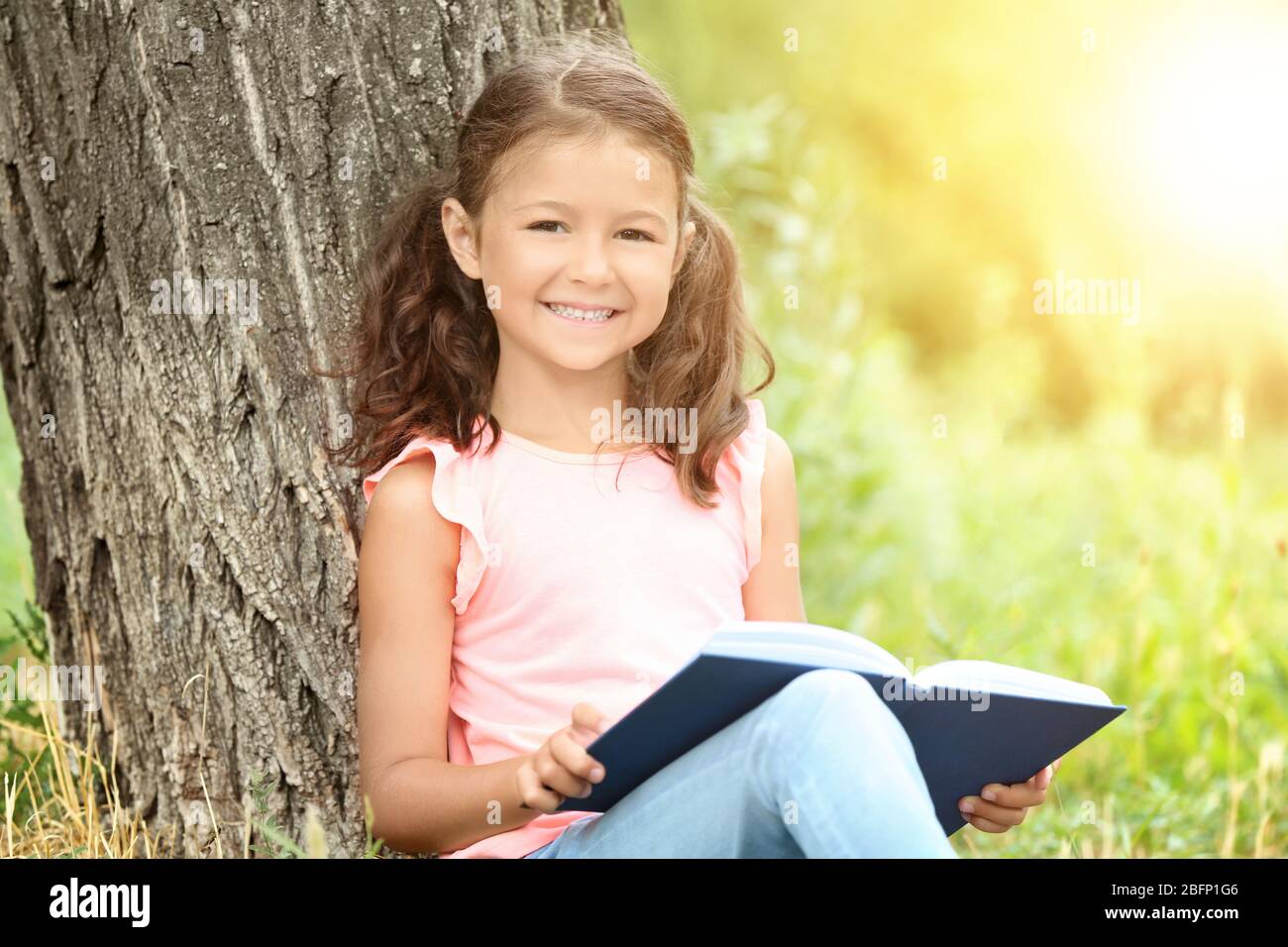Cute little girl reading book in park. Preparation of homework ...