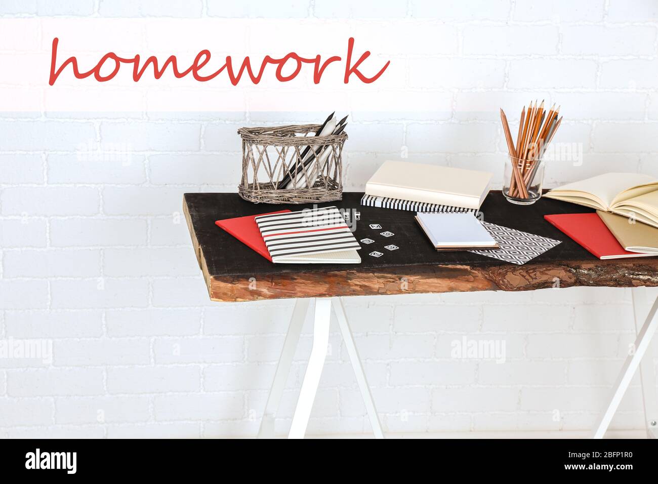 Desk with school supplies and word HOMEWORK on brick wall background ...