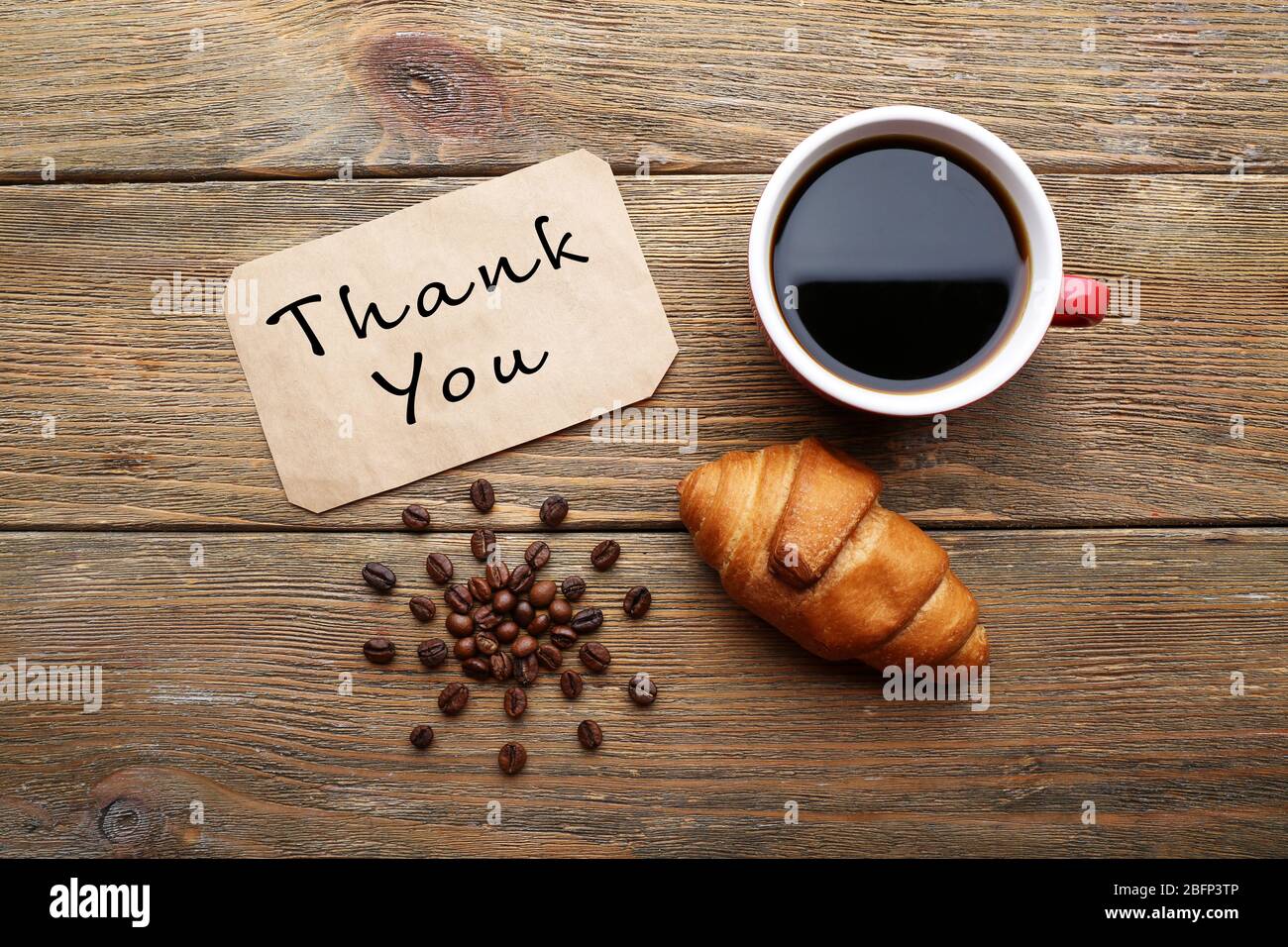 Cup of coffee, fresh croissant and card with text Thank You on wooden ...