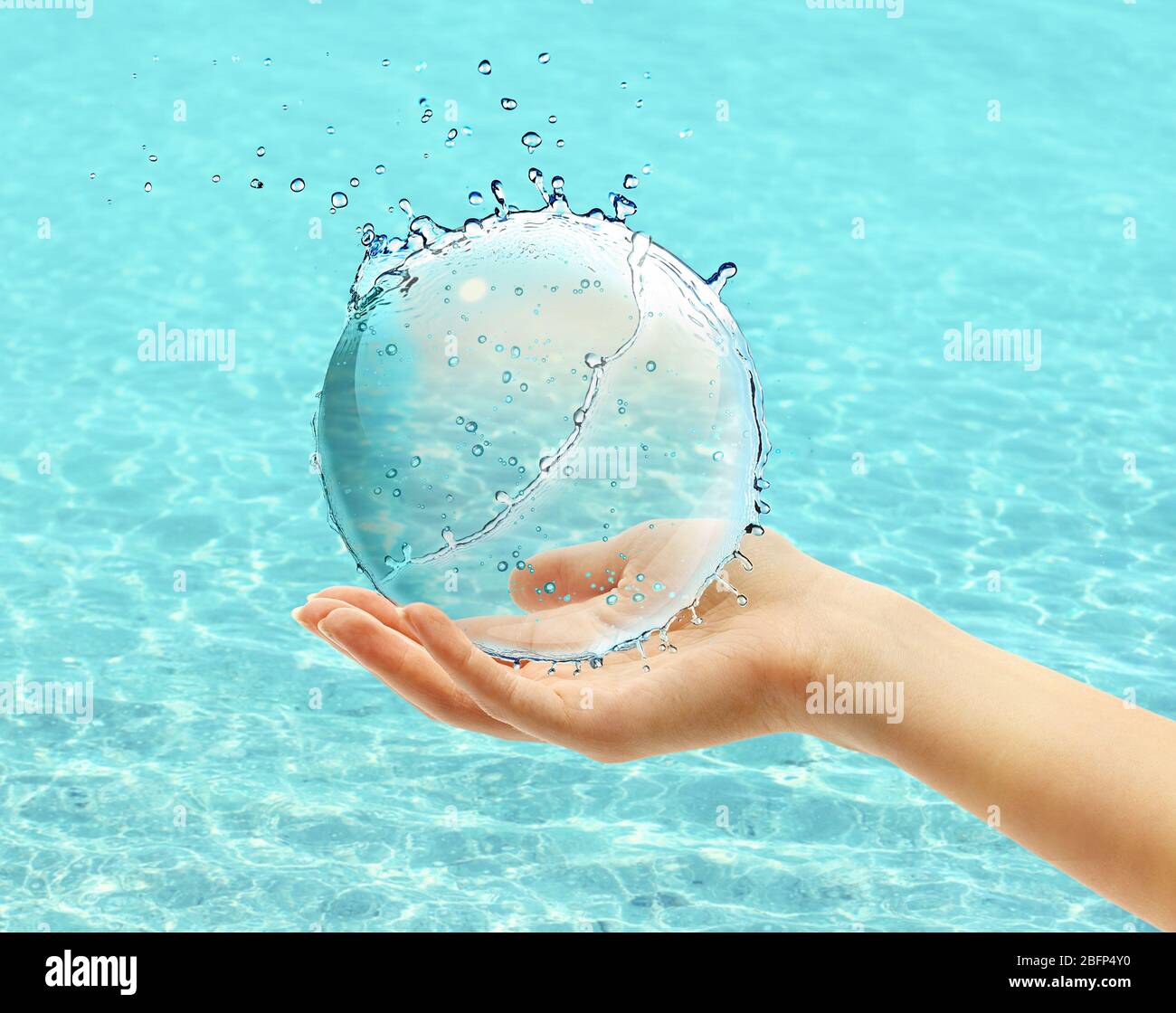 Female hand holding abstract water ball splash on blue water background ...