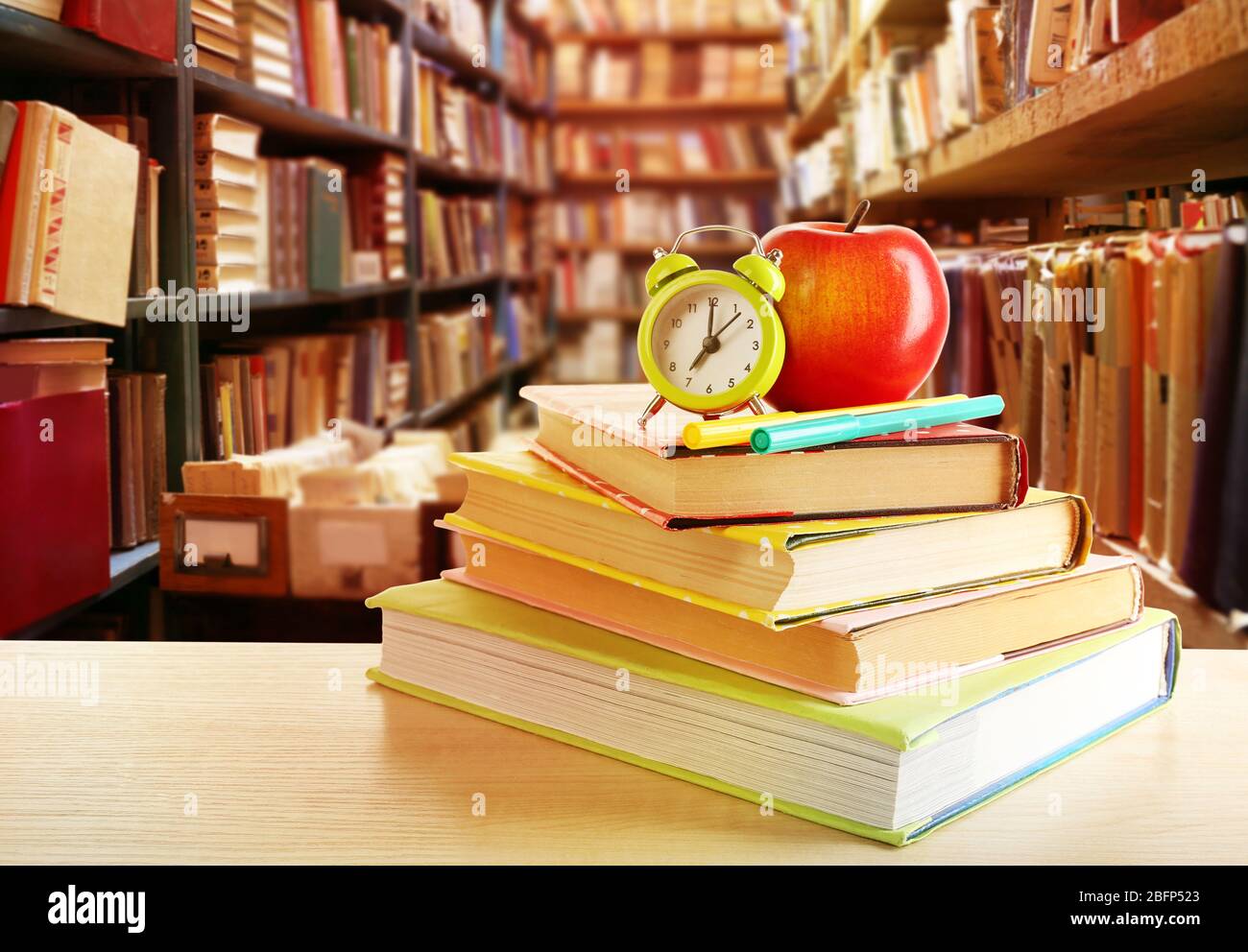 Books, alarm clock and apple on blurred library background Stock Photo ...