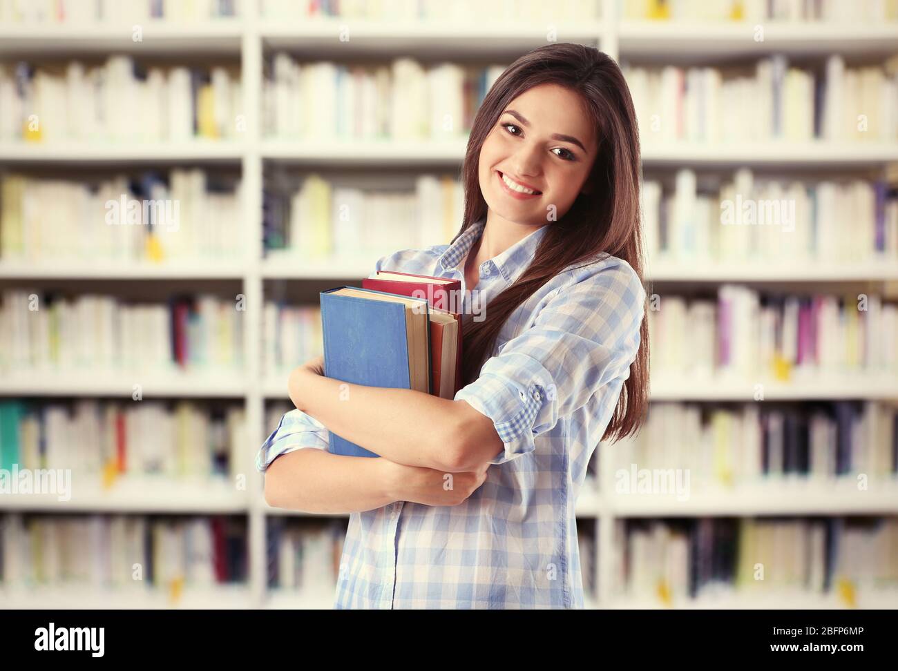 Beautiful young woman holding books on blurred book shelves background ...