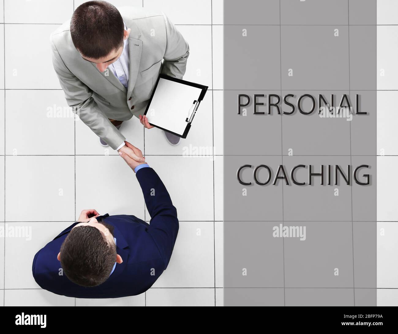 Personal coaching concept. Two businessmen shaking hands on grey ...